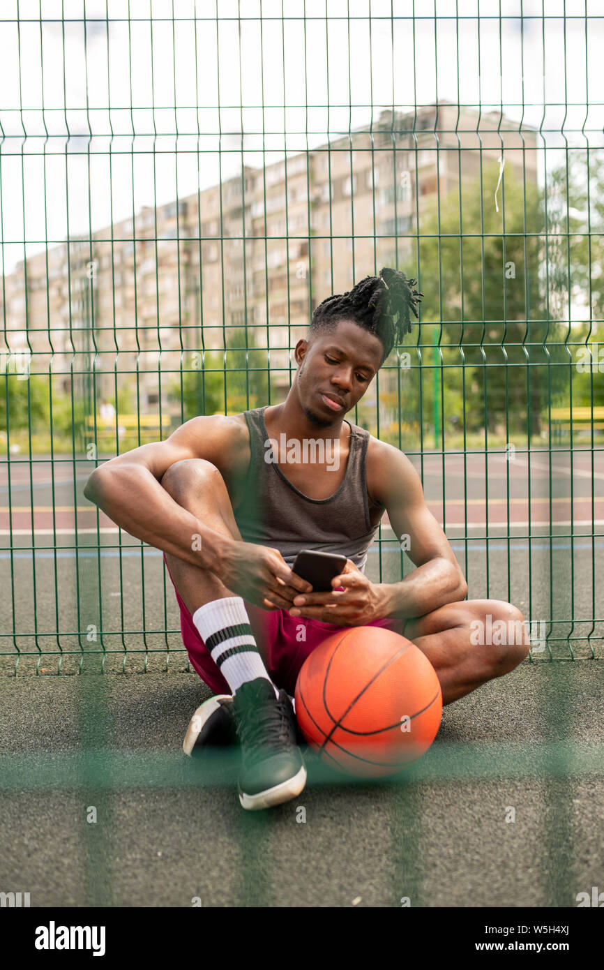 Restful African guy in sportswear scrolling or texting in smartphone ...