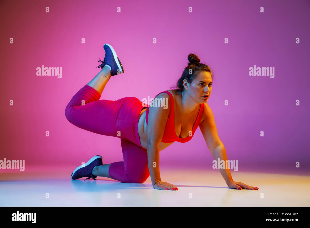 Young caucasian plus size female model's doing exercises on gradient ...