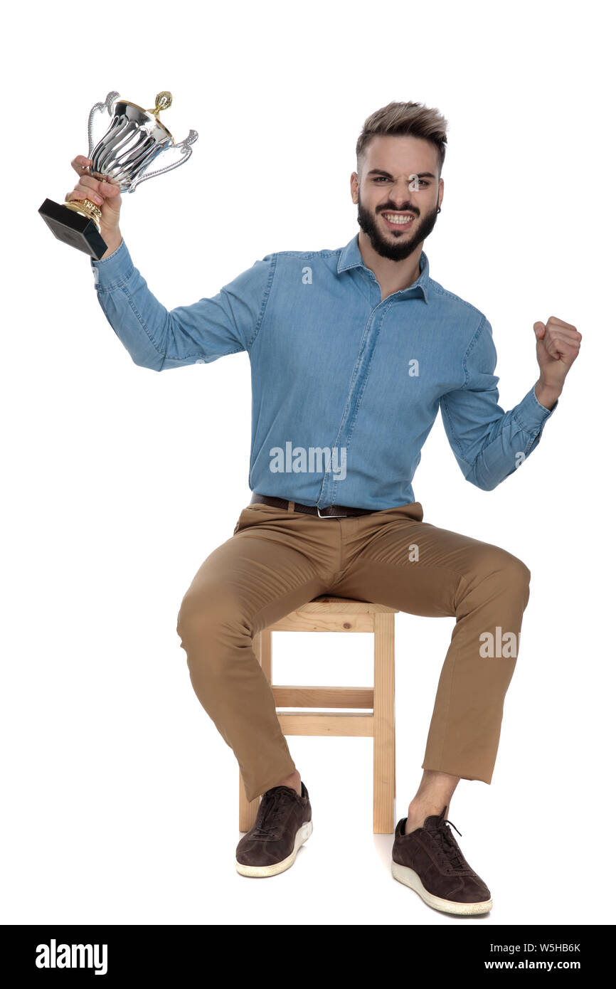 seated attractive man celebrating win with trophy cup up in the air on ...