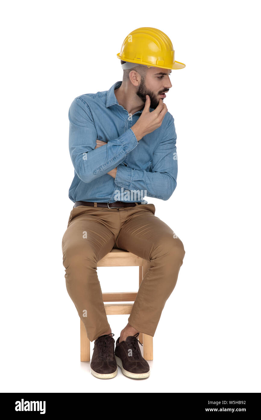 seated fashion man with yellow safety helmet thinking with folded arms ...