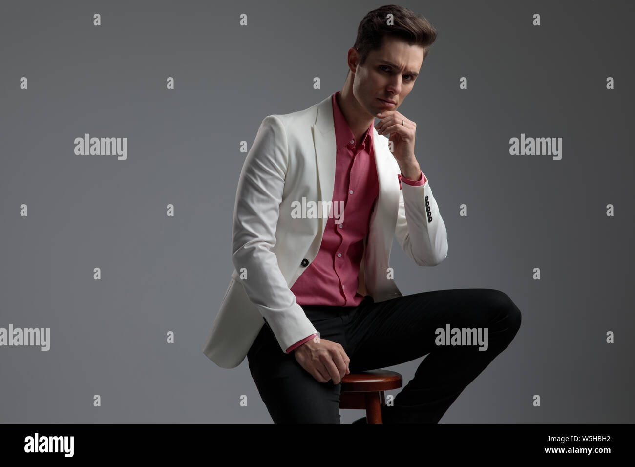 side view of a thinking man in suit holding his hand at chin on grey ...