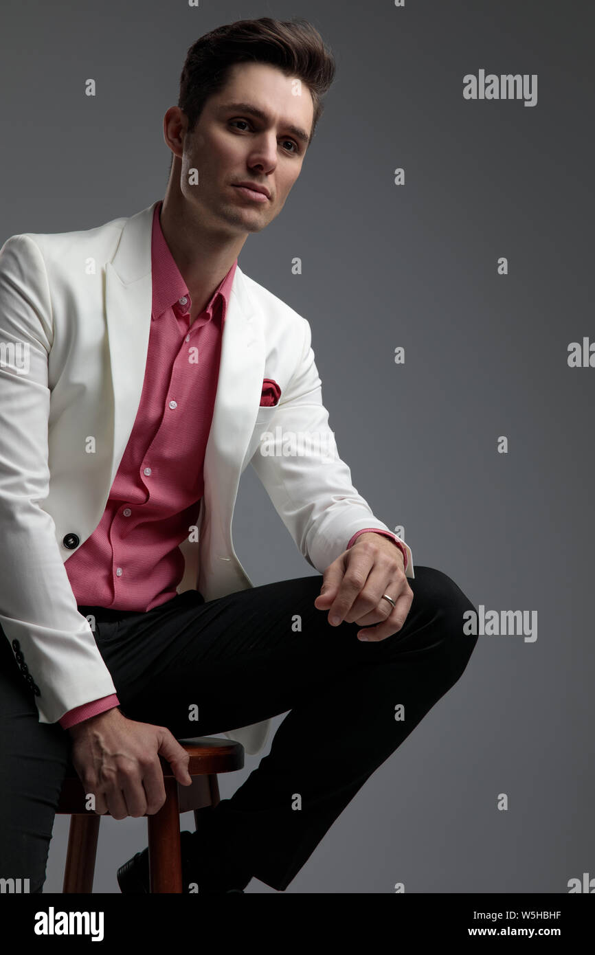 seated elegant man in suit resting his arm on leg while looking away on ...