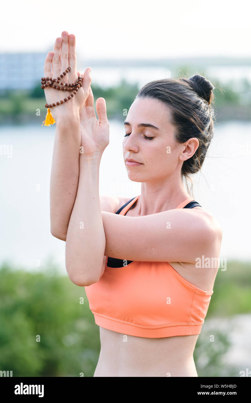 Peaceful young woman with closed eyes twisting arms while doing eagle ...