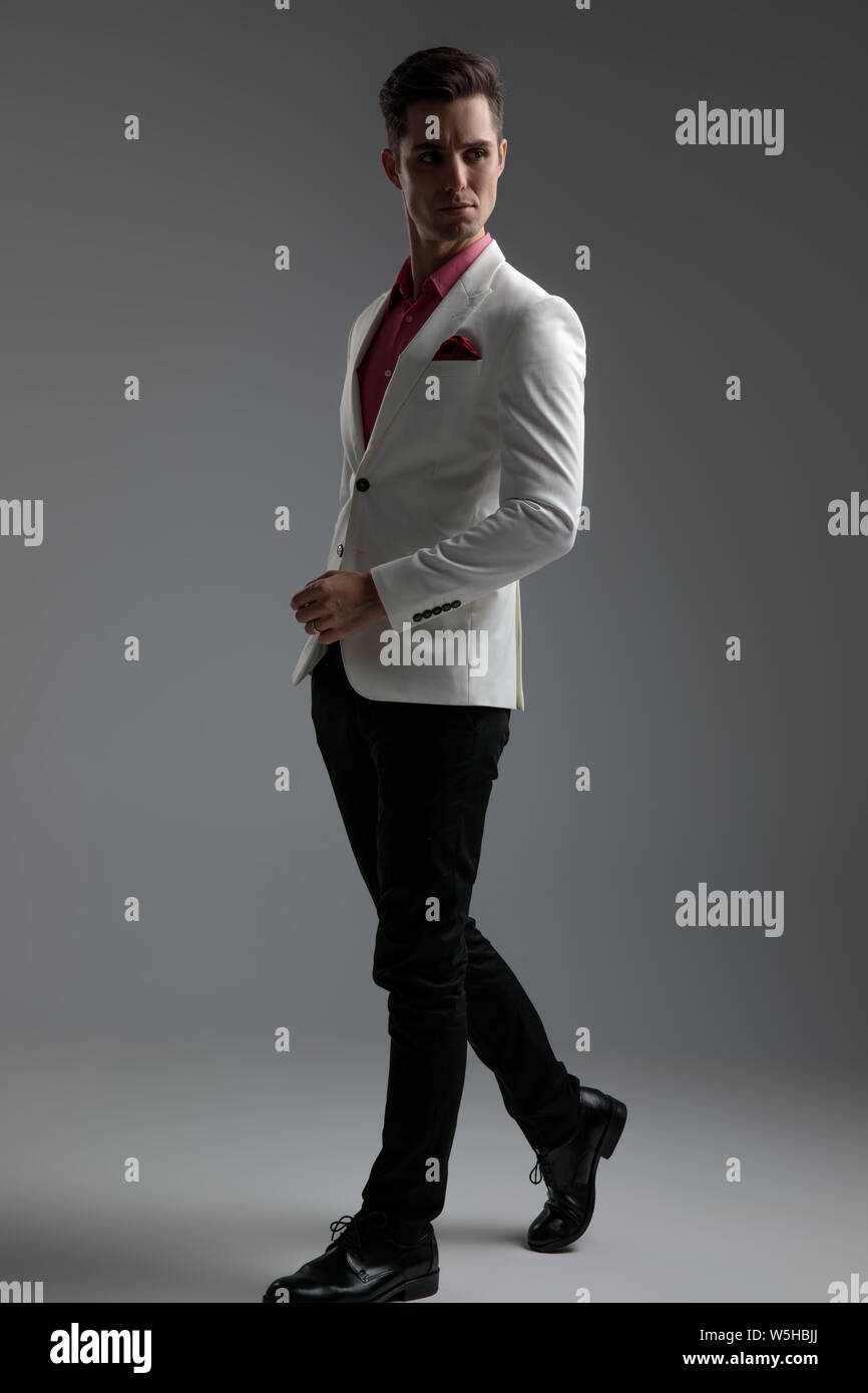 side view of a fashion man in suit walking with hand in pocket and ...