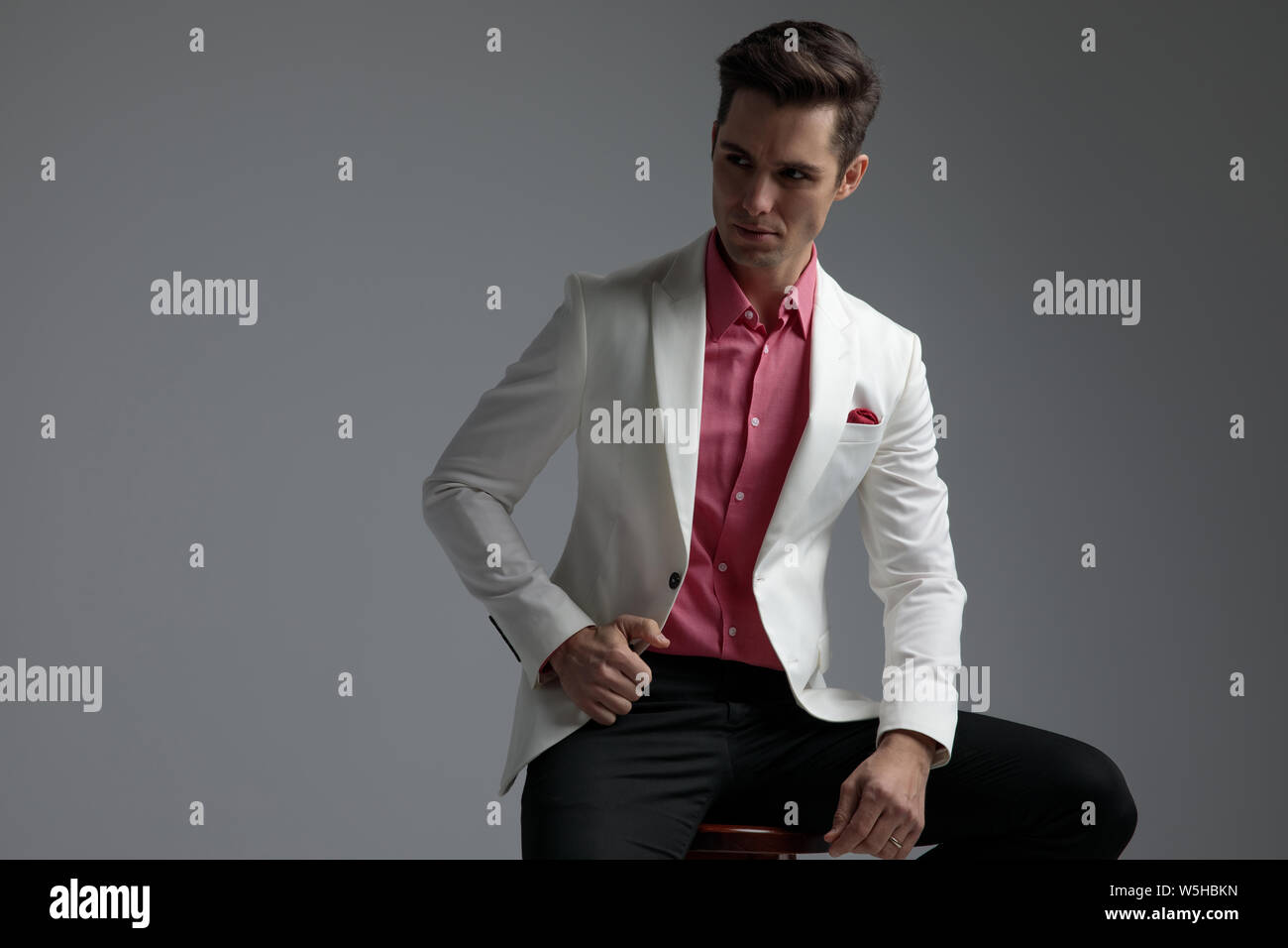 seated smart man in suit adjusting his lounge jacket while looking away ...