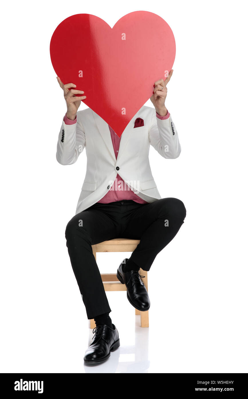 seated modern man holding a big red heart over his face on white ...