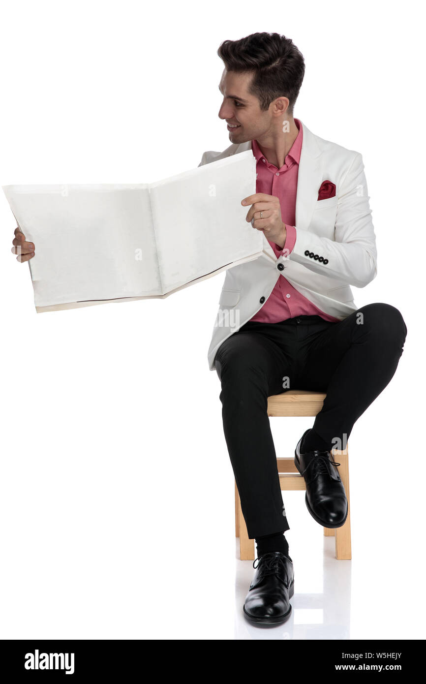 smiling elegant man showing newspaper to side while sitting on chair on ...