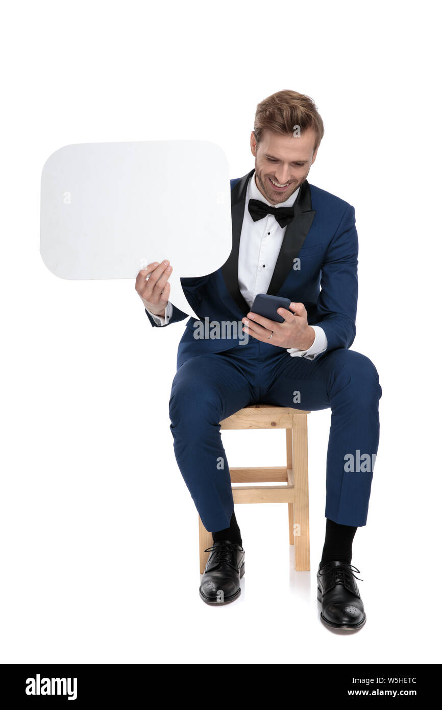 seated attractive man in blue costume texting on mobile phone while ...