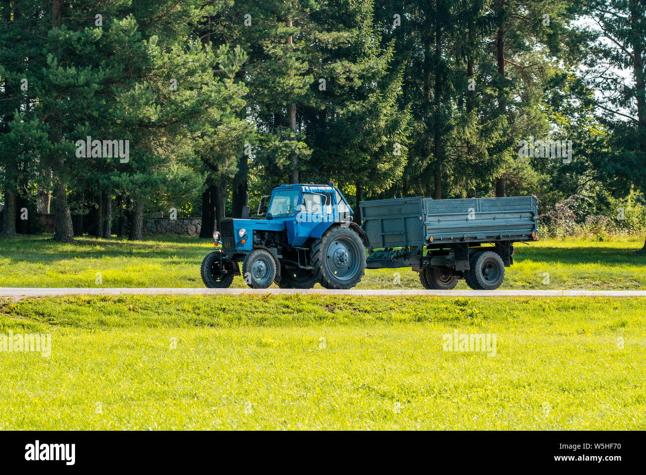 Tractor with a trailer goes on country road Stock Photo - Alamy