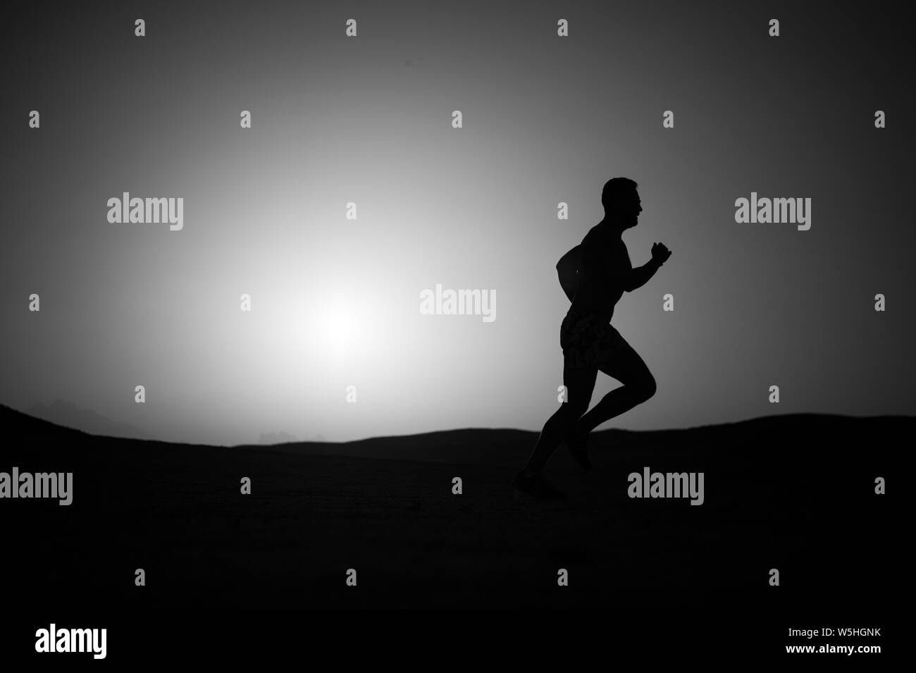 man silhouette, running guy on sunset fiery sky background in mountain ...