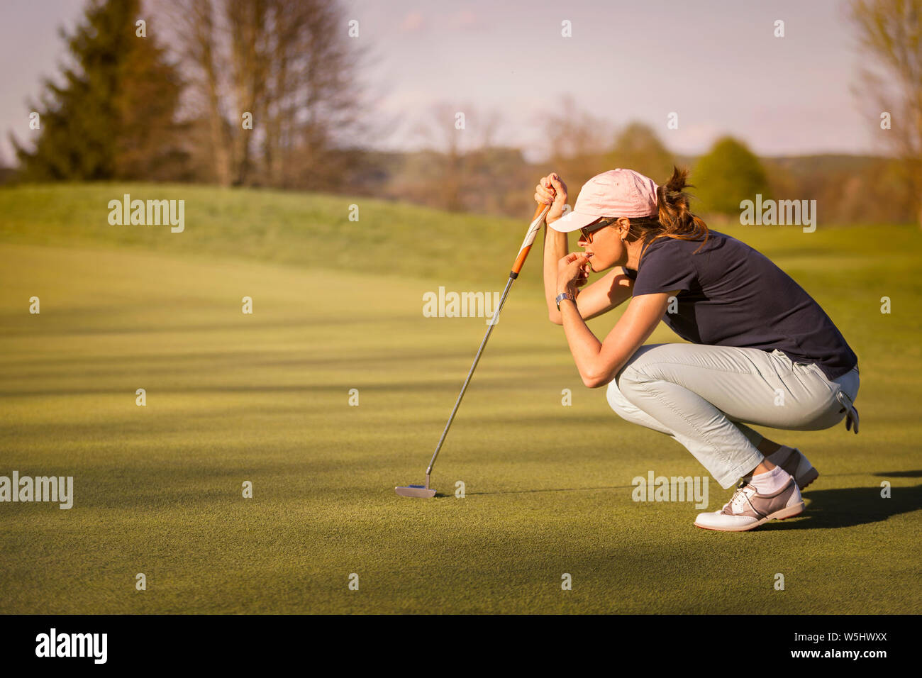Female golf player squatting on green Stock Photo - Alamy