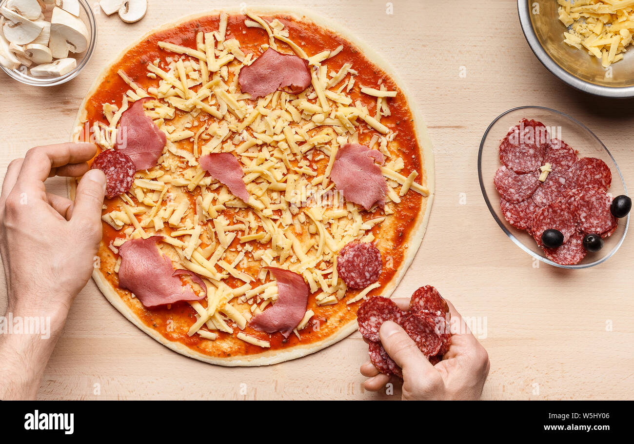 Chef putting ham and salami slices on raw pizza base Stock Photo - Alamy
