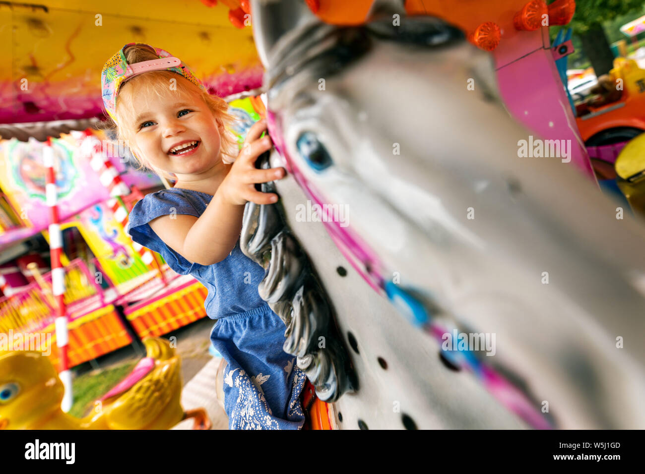 happy smiling little girl sitting on horse carousel at amusement park ...
