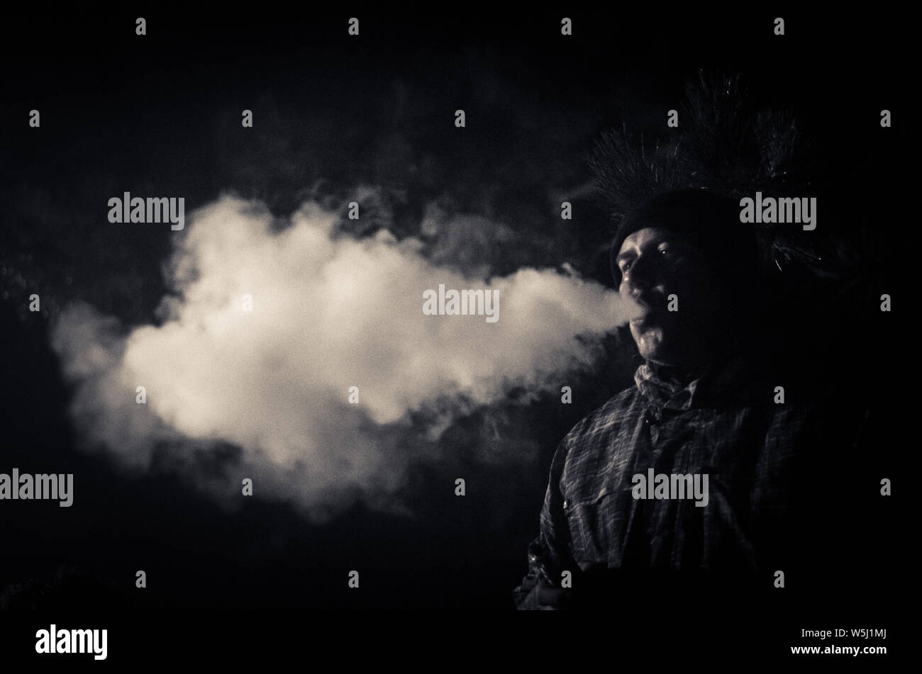 adult man smoking at night making a big smoke effect in back light ...