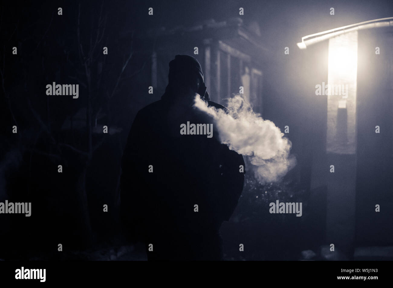 adult man smoking at night making a big smoke effect in back light ...