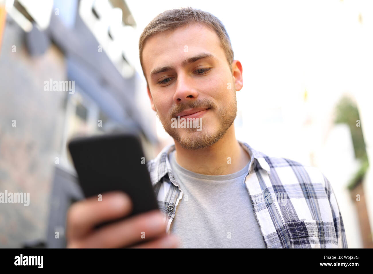 Serious man is walking using a smart phone in the street of an old town ...
