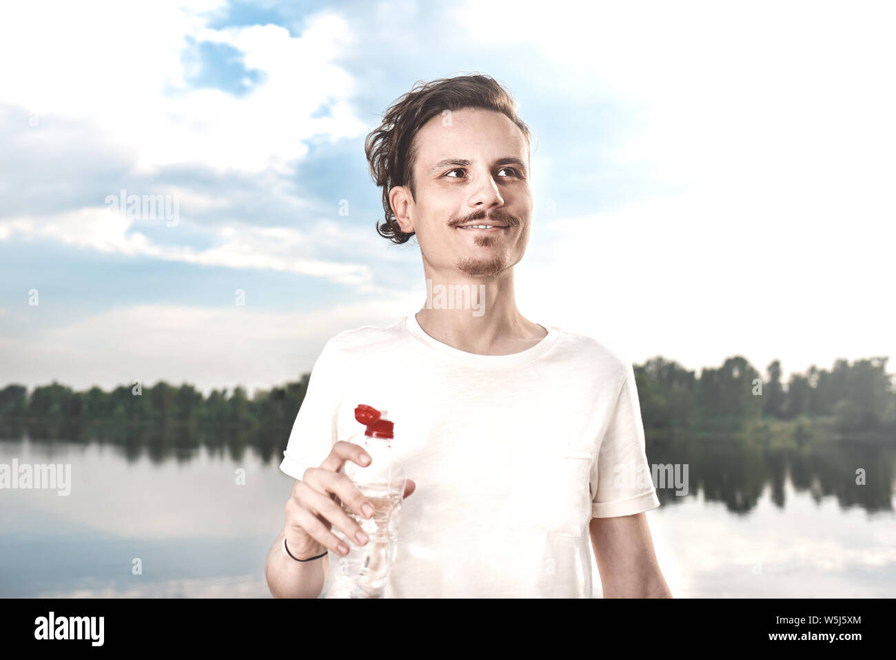 young guy drinks fresh water against of the lake and the forest ...