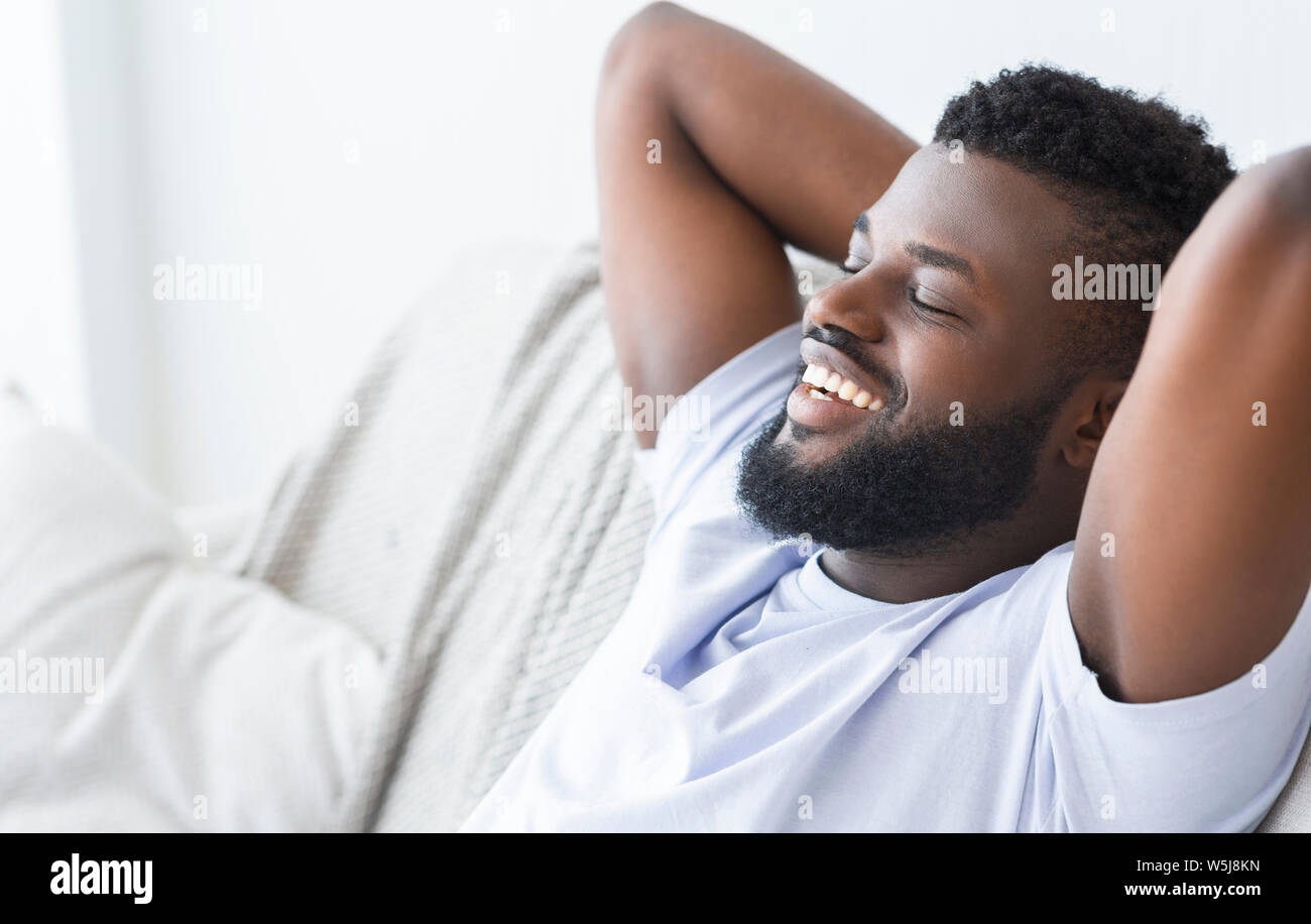 Pleased black man relaxing at home on couch Stock Photo - Alamy