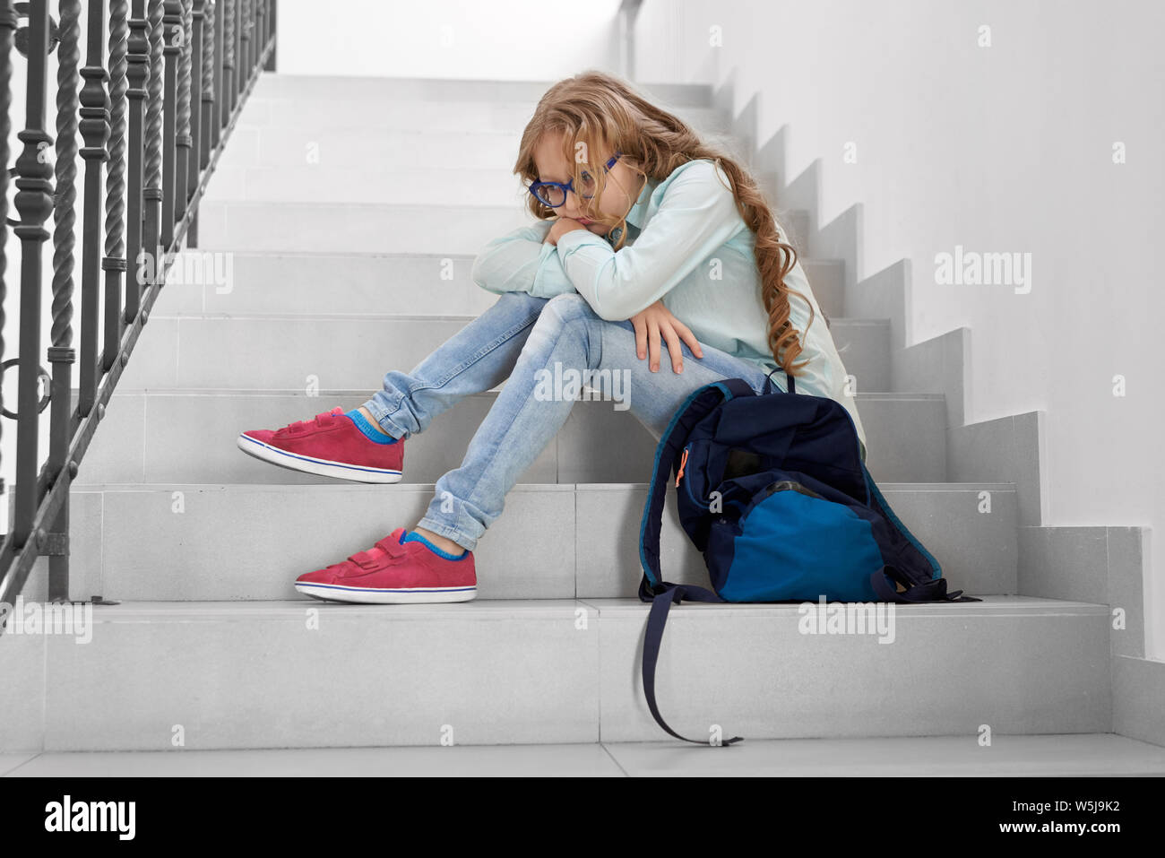 Side view of blonde school girl sitting on stairs and hiding face from ...