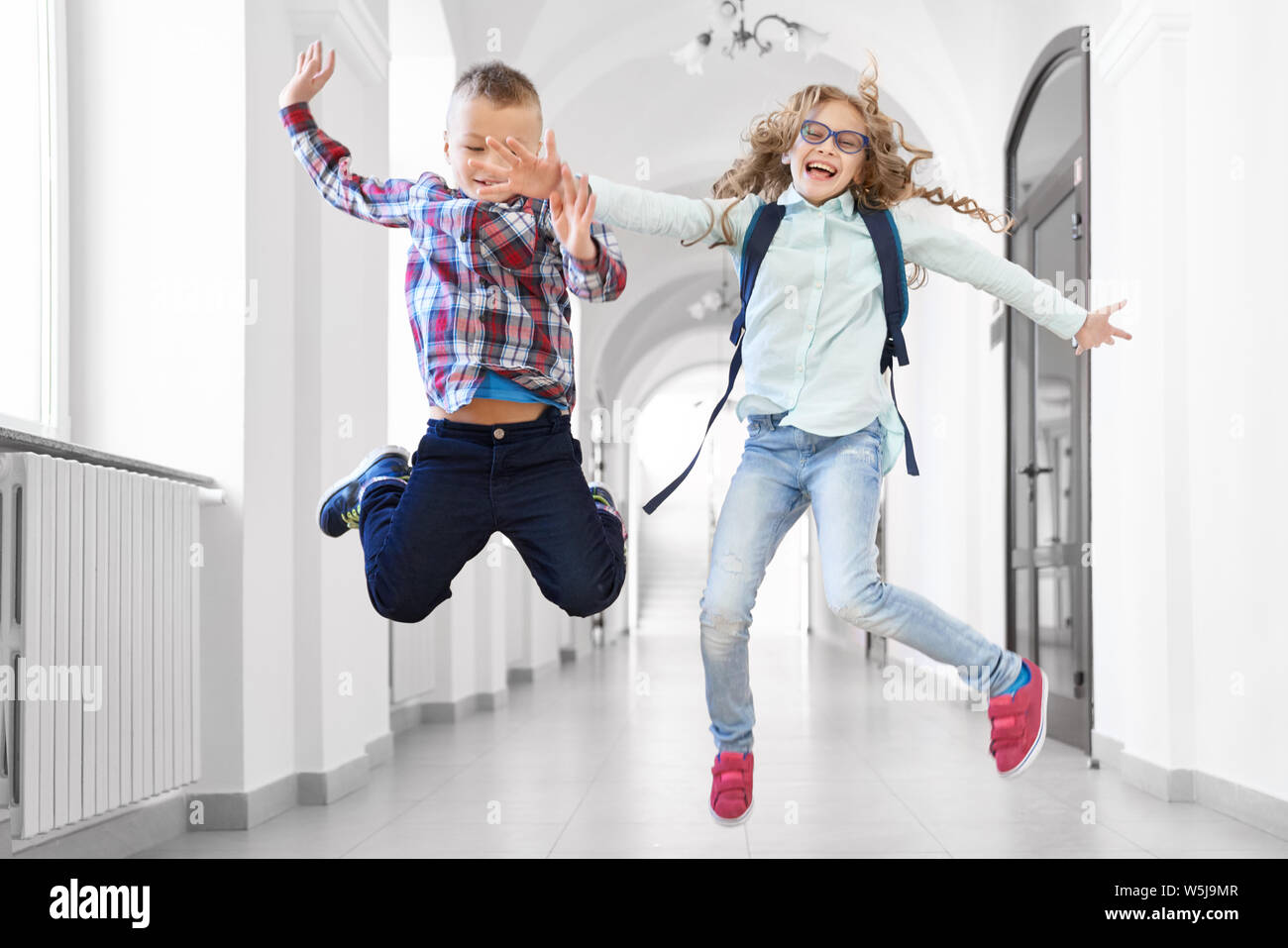 Happy pupils boy and girl high jumping up at school corridor and ...