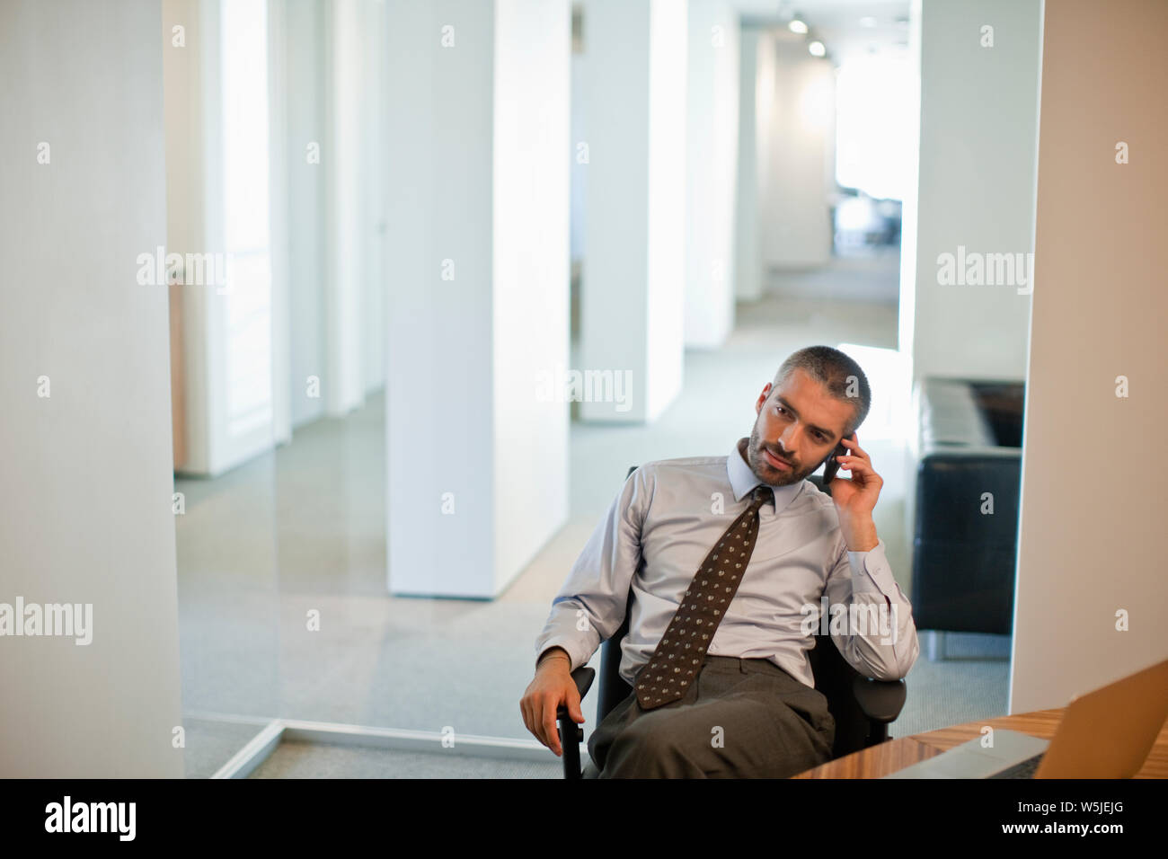 Businessman leans back on chair listening on his cellphone Stock Photo ...