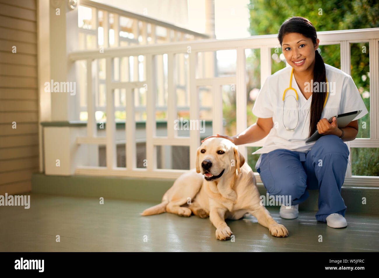 Young female nurse playing with a dog on the verandah of someone's home ...