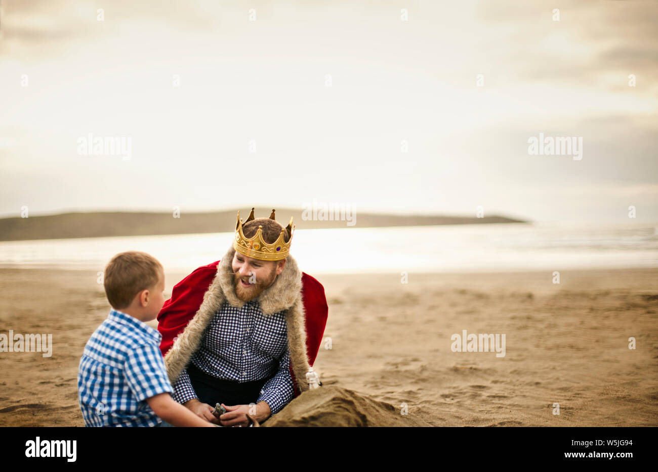 Mid-adult man wearing robe and crown while playing with his son at the ...