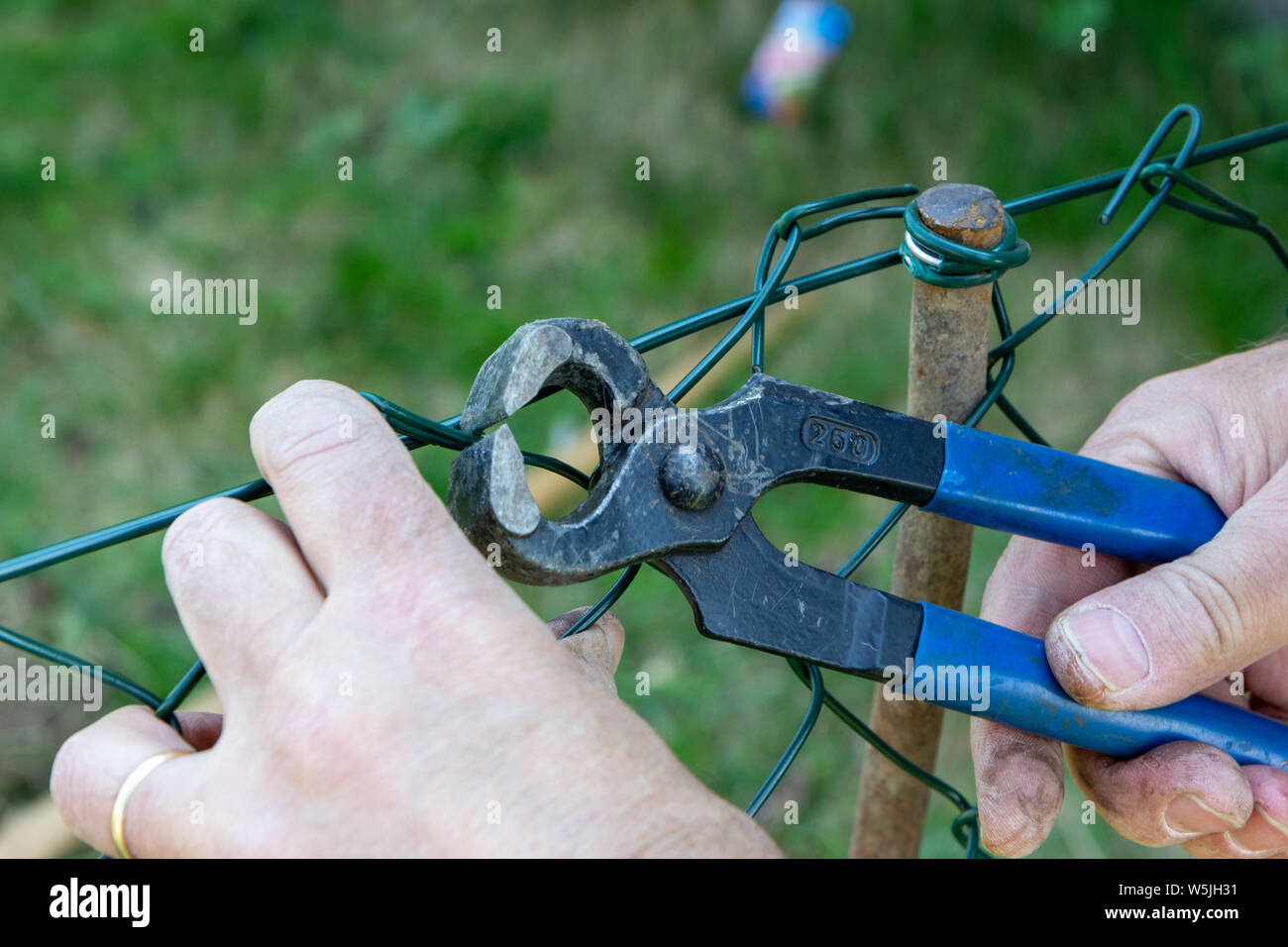 a man repairing a metal wire fence with pliers Stock Photo - Alamy