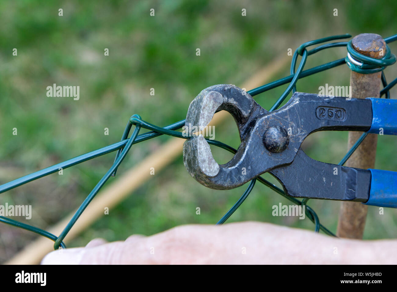 a man repairing a metal wire fence with pliers Stock Photo - Alamy