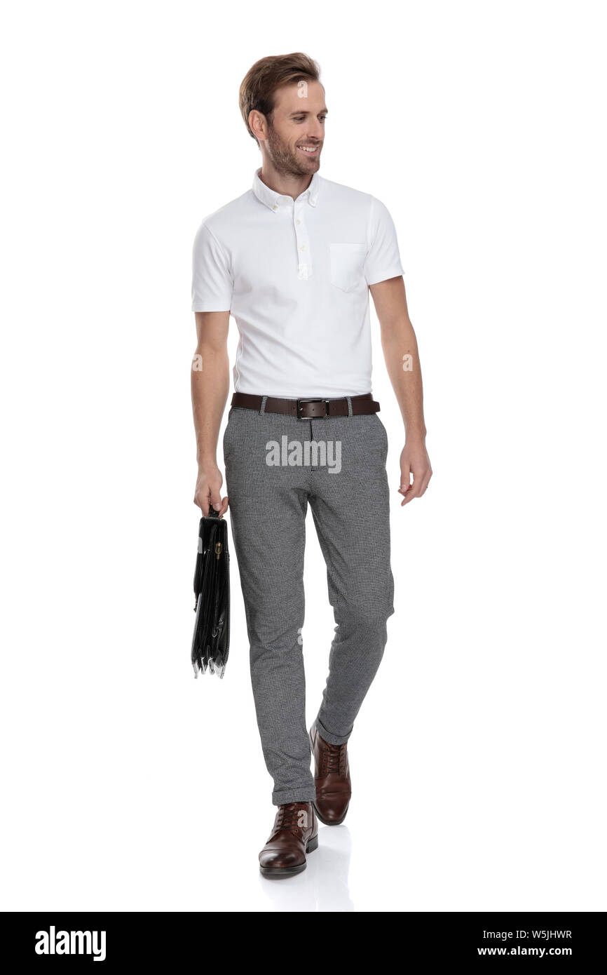 happy young smart casual man walking with suitcase and looks to side on ...