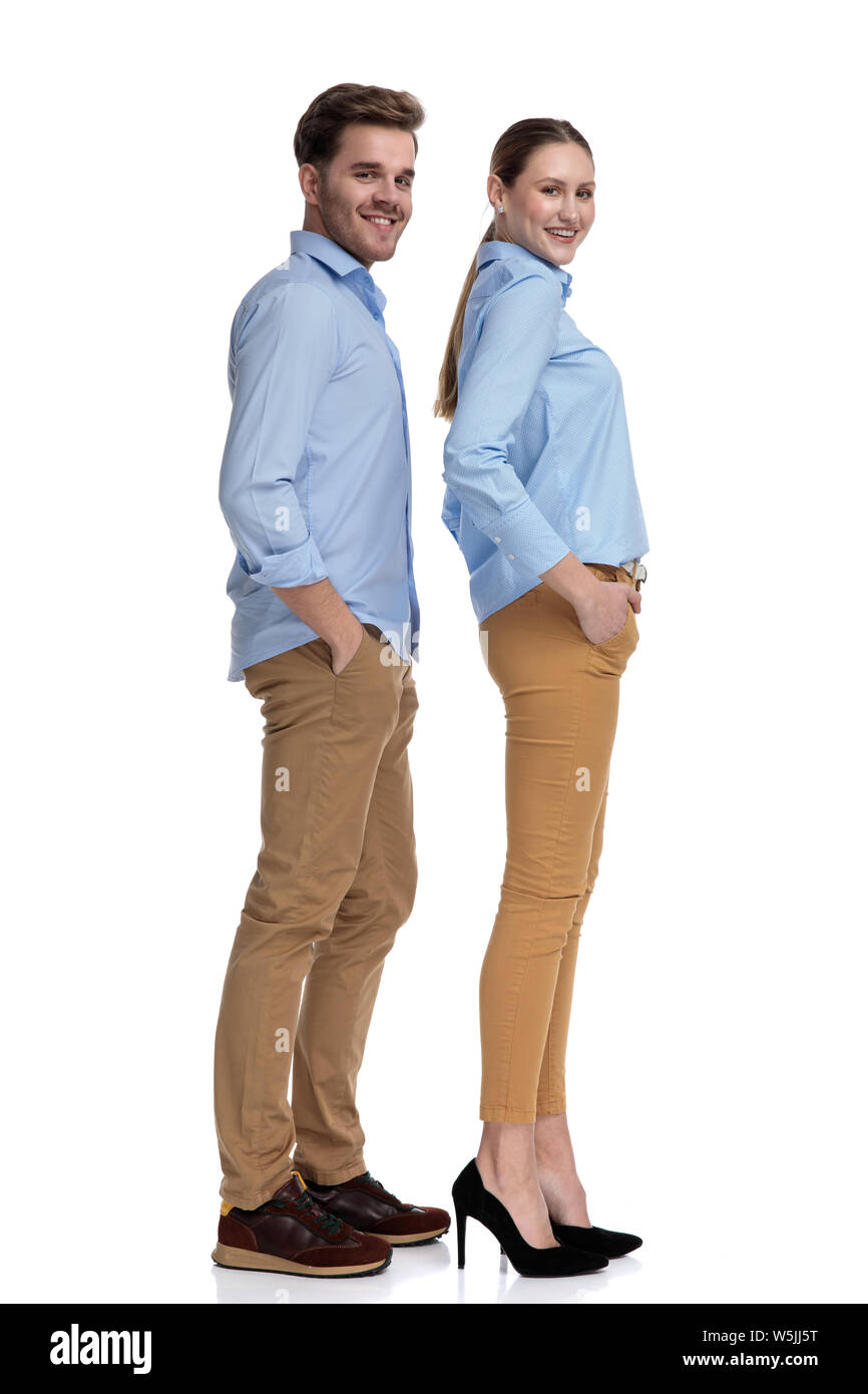side view of smiling man and woman with hands in pockets standing on ...