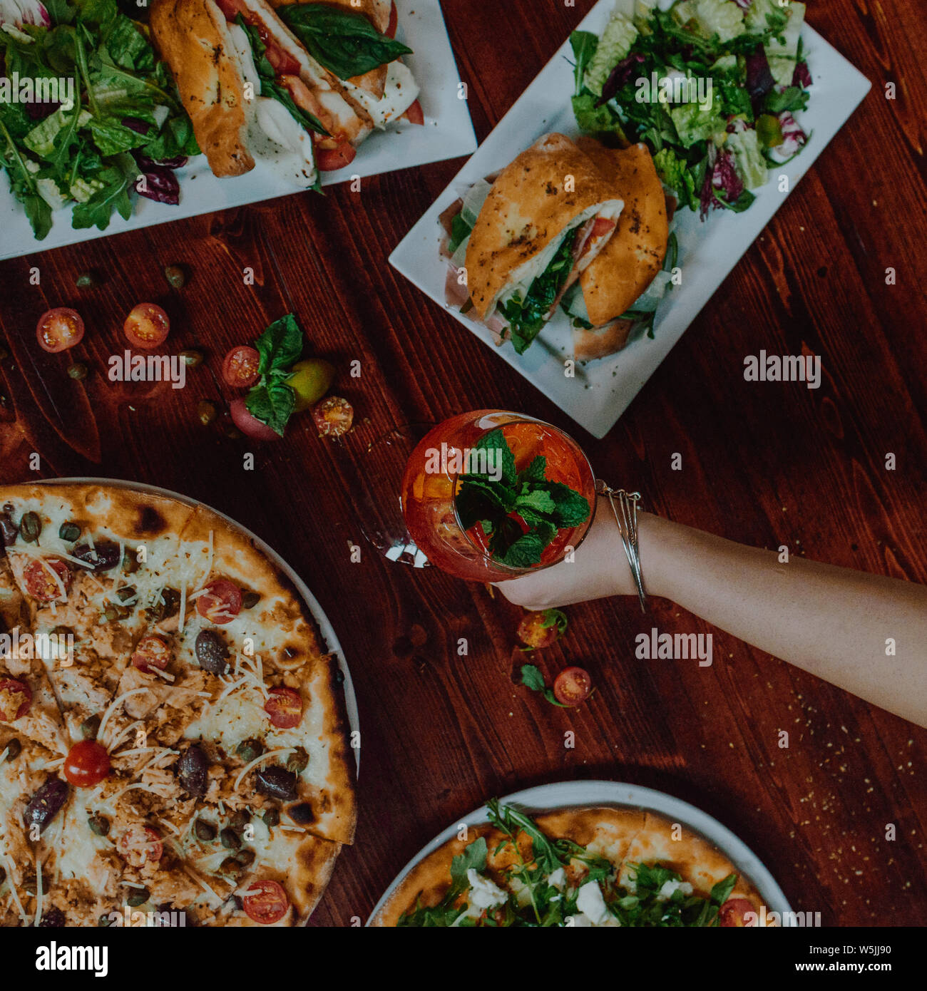 Hand reaching for cocktail on a table with food Stock Photo - Alamy