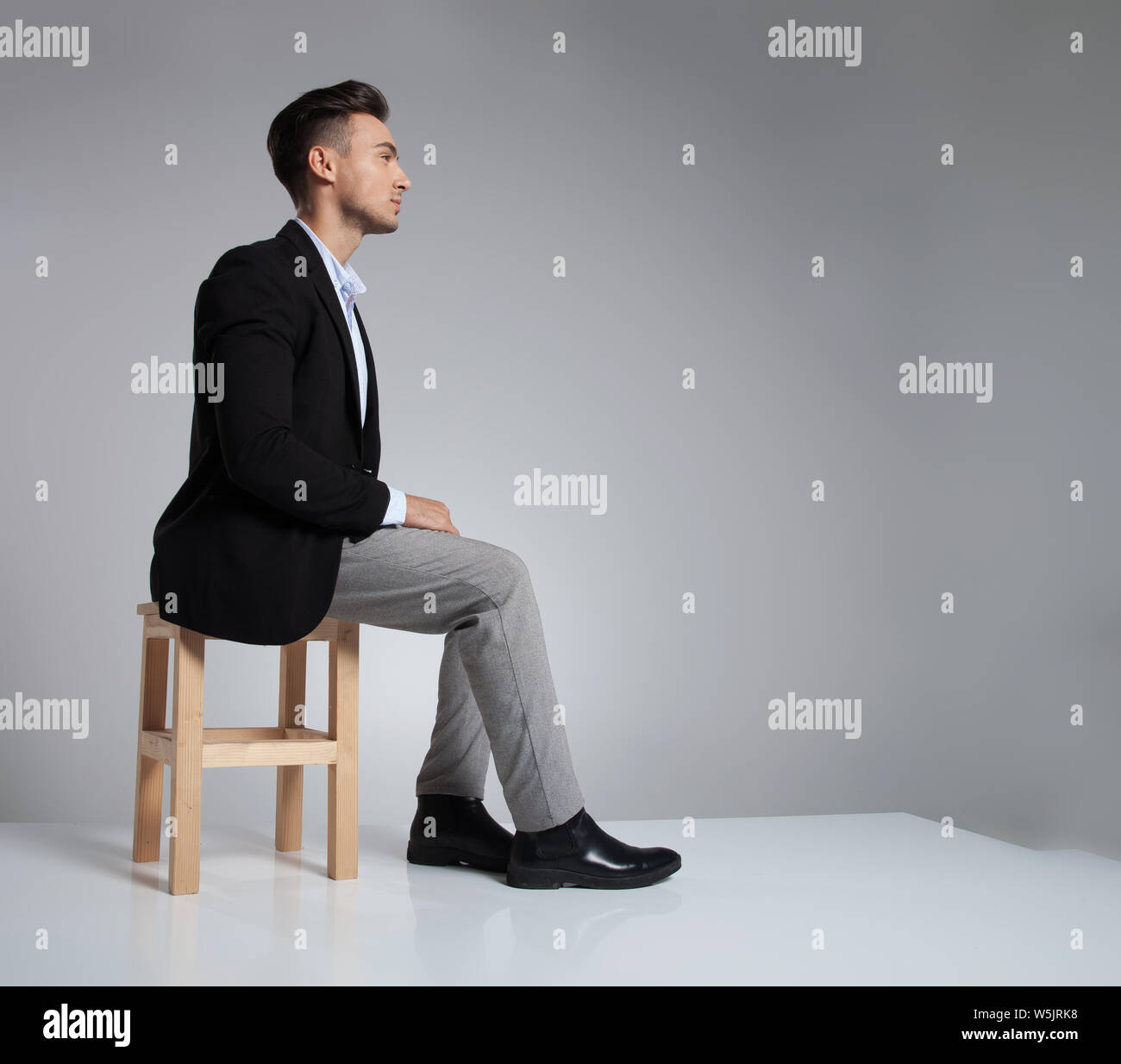 side view of young businessman sitting on wooden chair on light grey ...