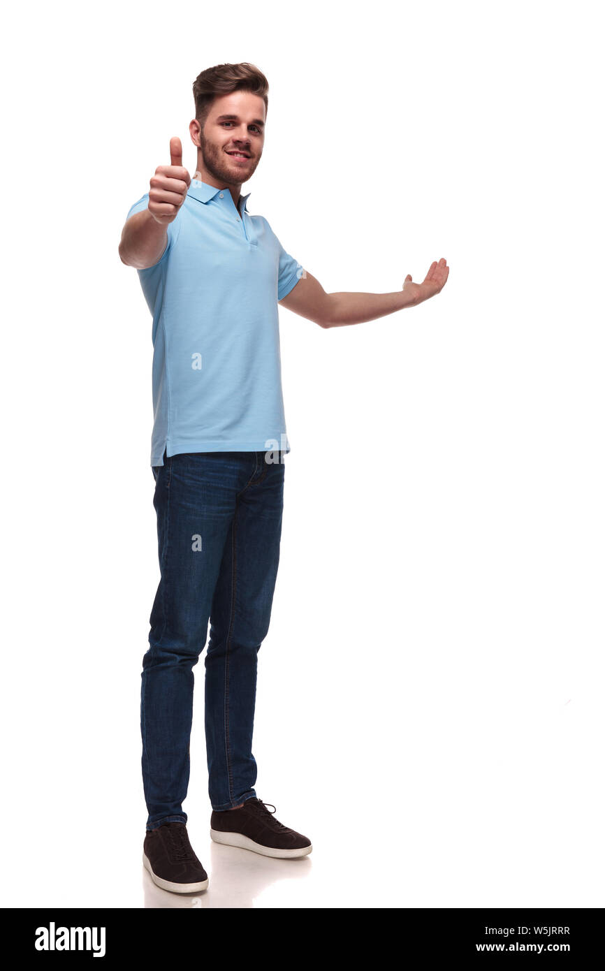 casual man presents to side while making thumbs up sign and standing on ...