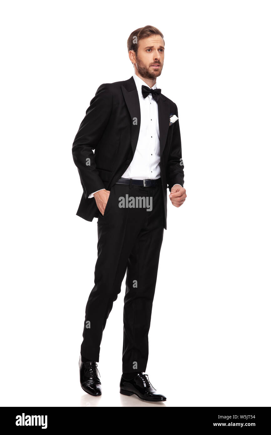 curious businessman in black suit looks to side while walking with hand ...