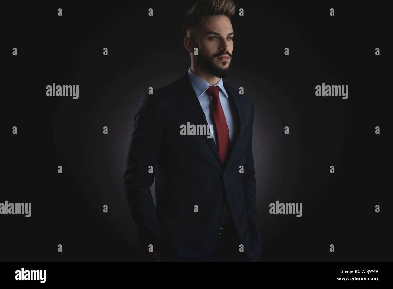 curious businessman in navy suit looks to side while standing on black ...