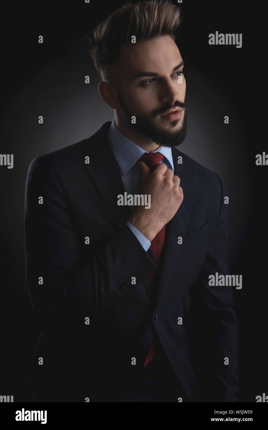 portrait of curious businessman in navy suit looking to side and fixing ...