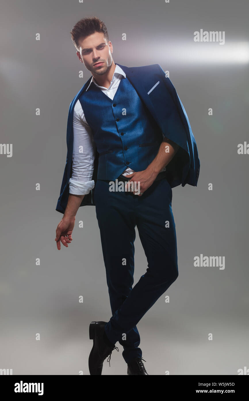 attractive young man wearing blue suit stands with legs crossed on ...
