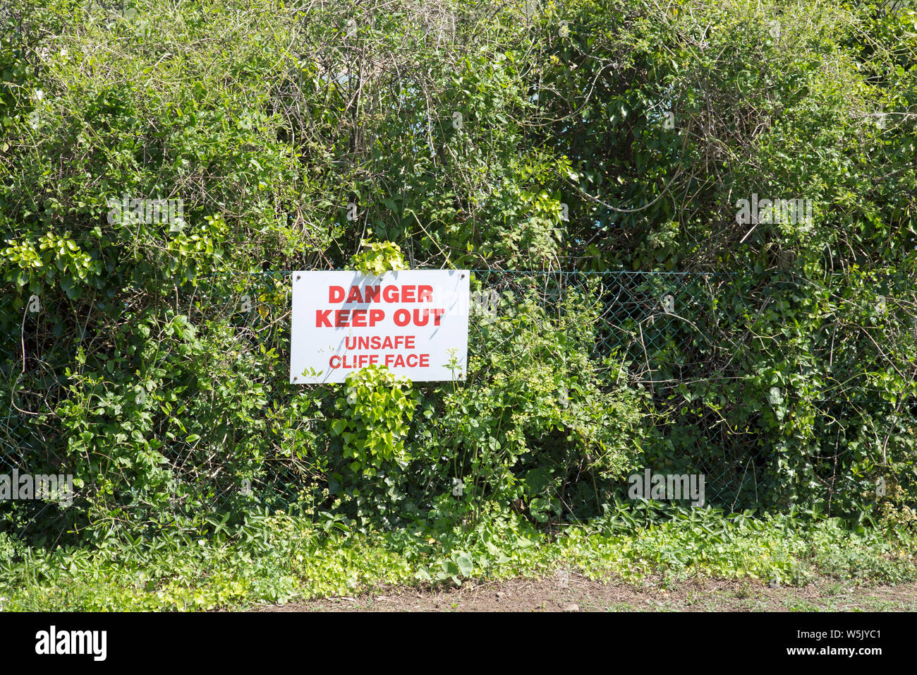 Green shrubbery surrounds a sign announcing "Danger, Keep out, Unsafe ...