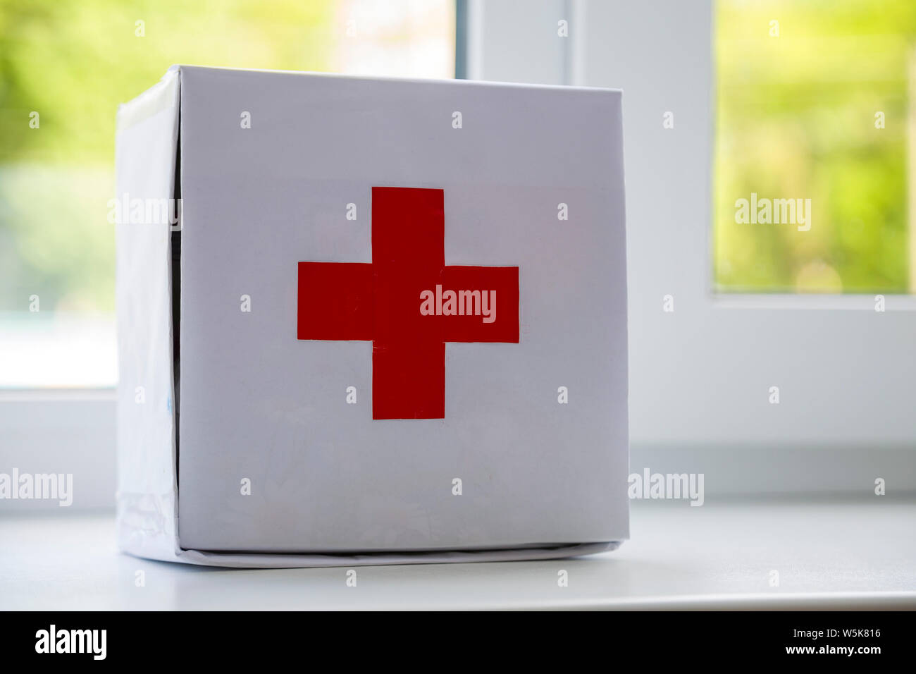 White first aid kit with red cross indoors on windowsill on blurred ...