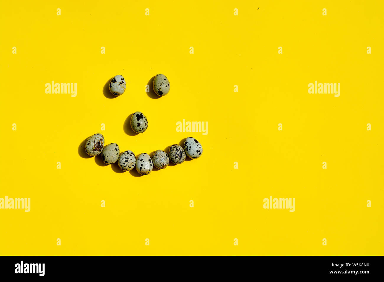 Set of group quail eggs form a smile face on a yellow background. Top ...