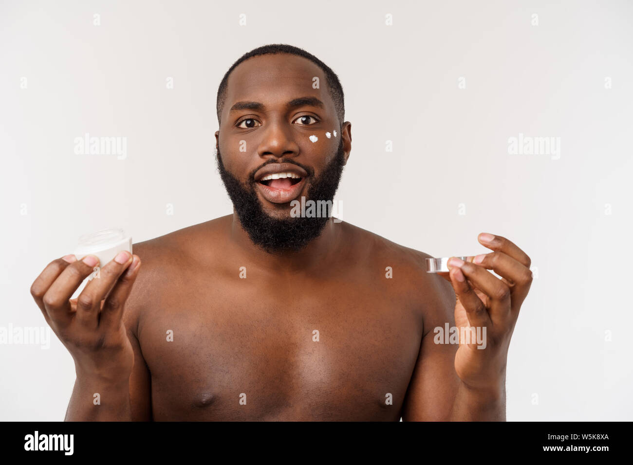 Smiling afro man applying cream on his face. Man's skin care concept ...