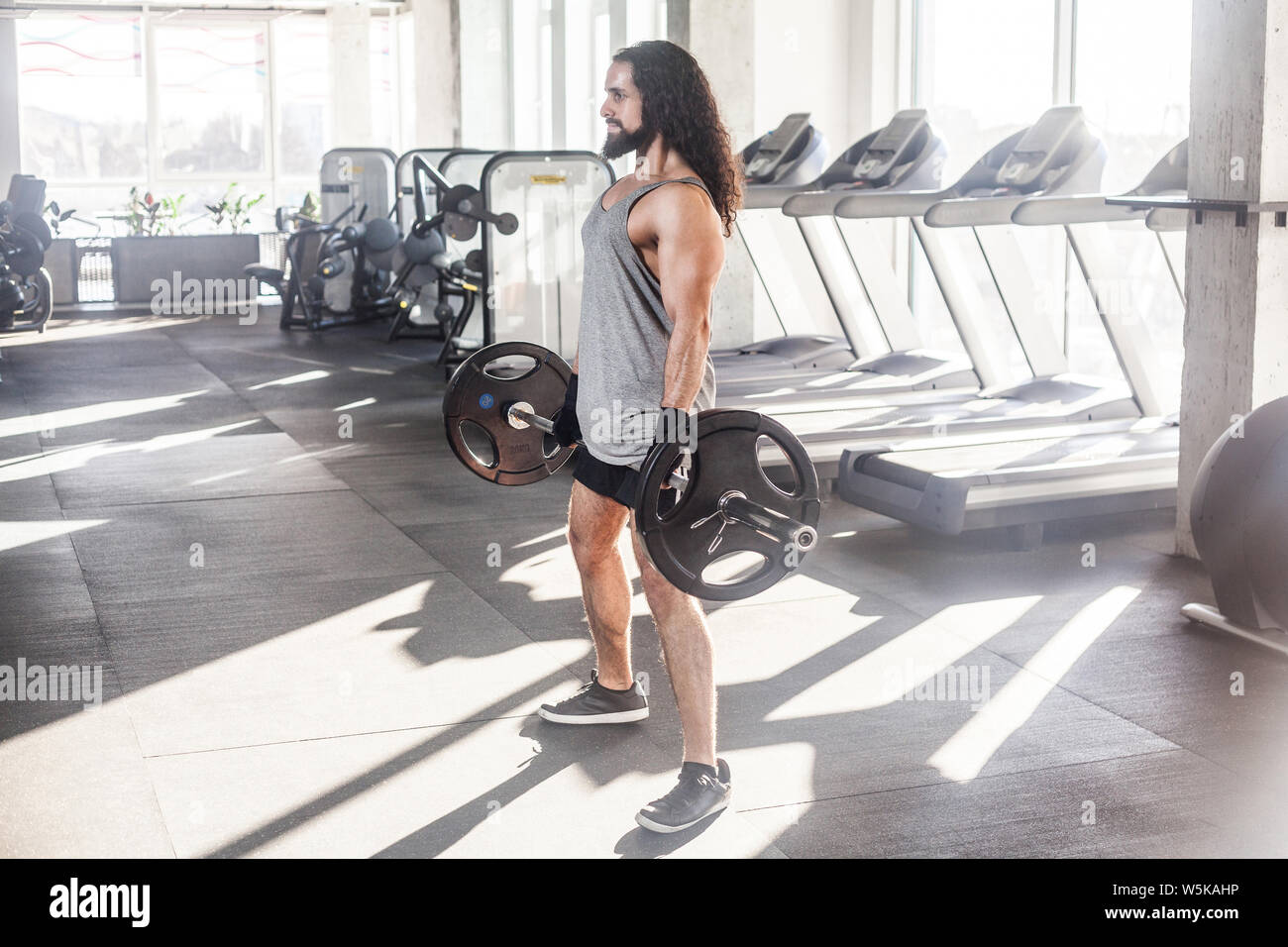 Side view portrait of young adult bodybuilder with long curly hair are ...