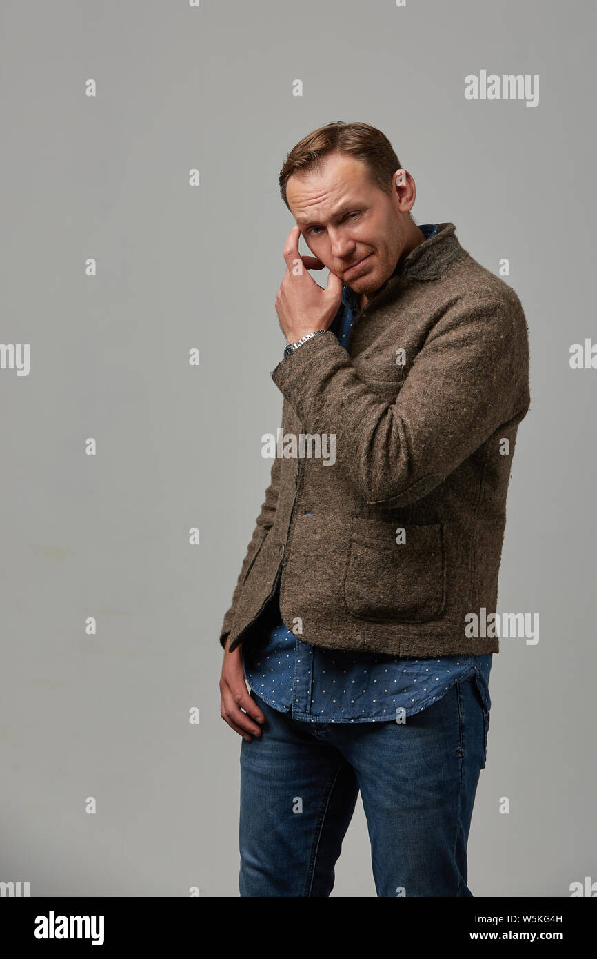 A man in casual clothing hides his face with his hands on a gray ...