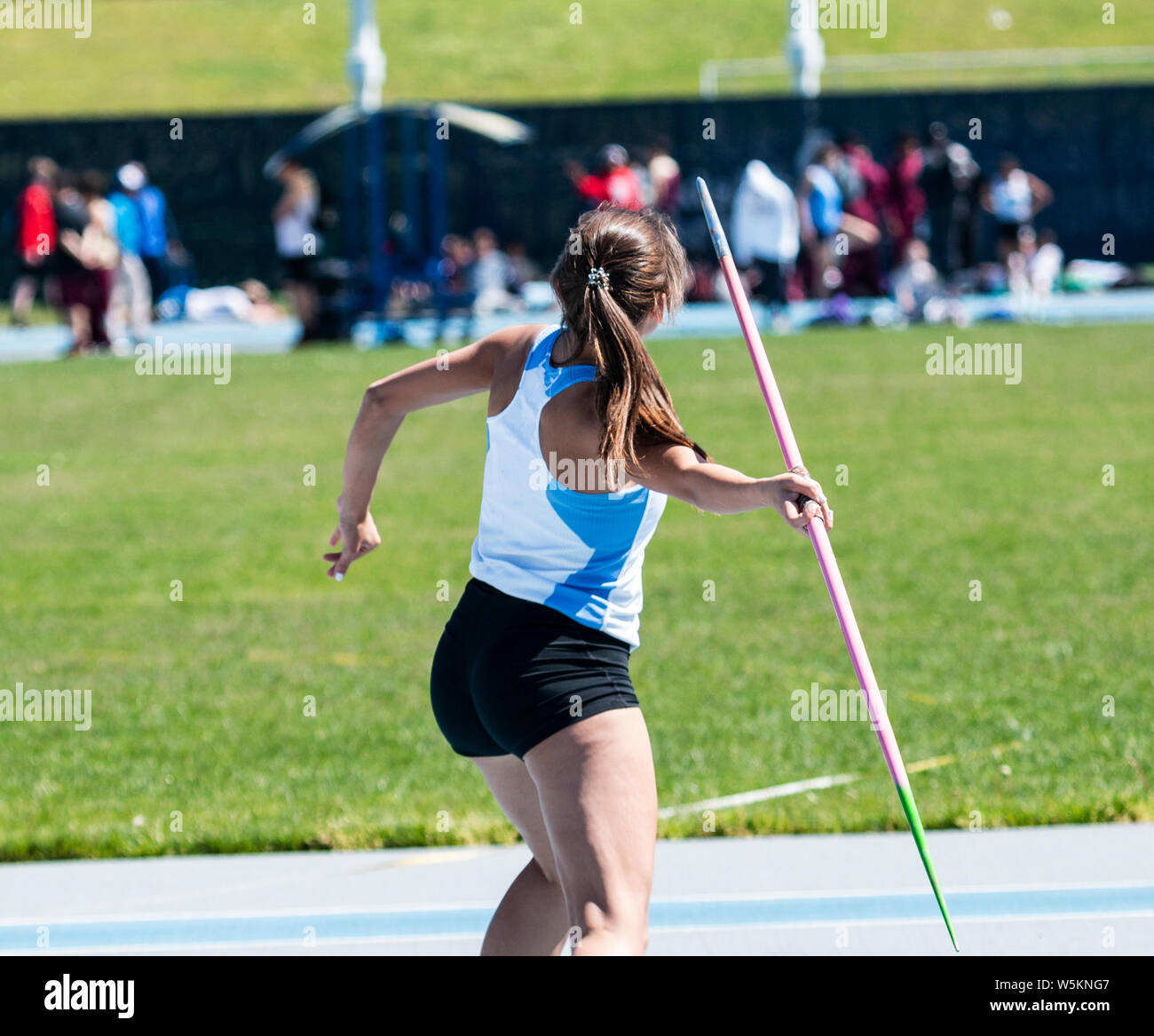 A rear view of a high school girl throwing a pink javelin onto a grass ...