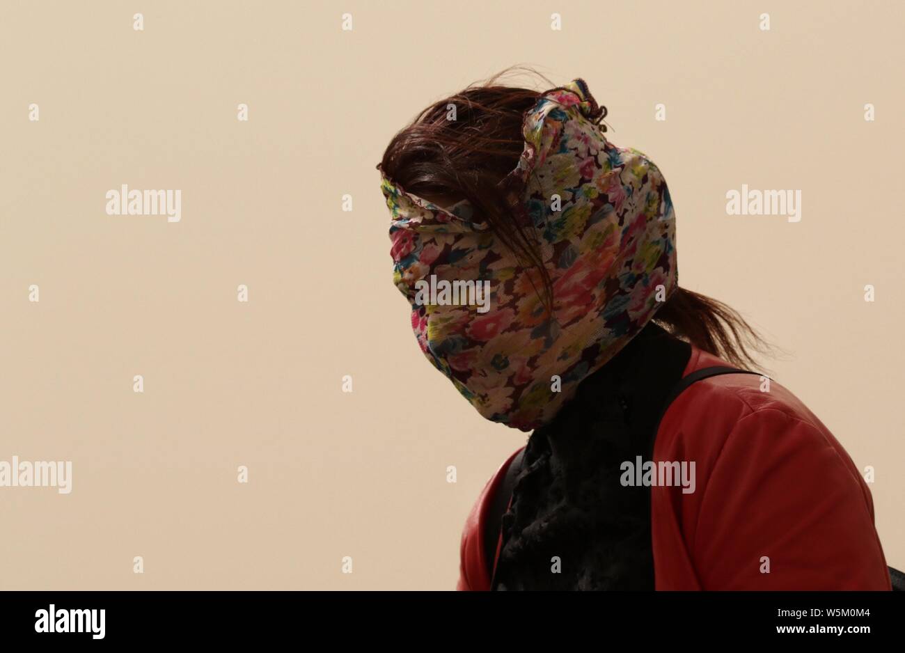 A pedestrian covers her head with a scarf against air pollution and ...