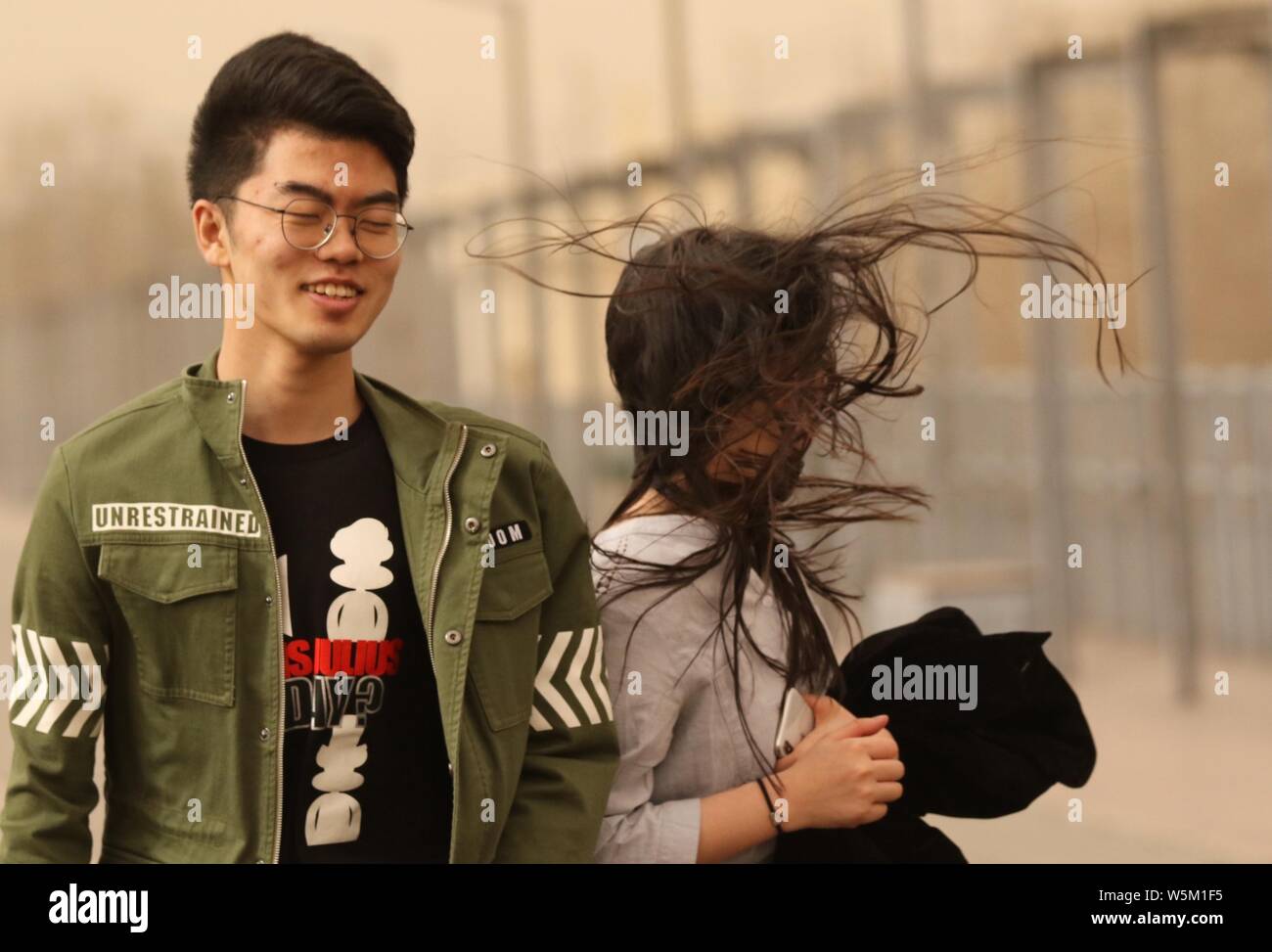 Pedestrians walk on a road against air pollution and strong wind in ...