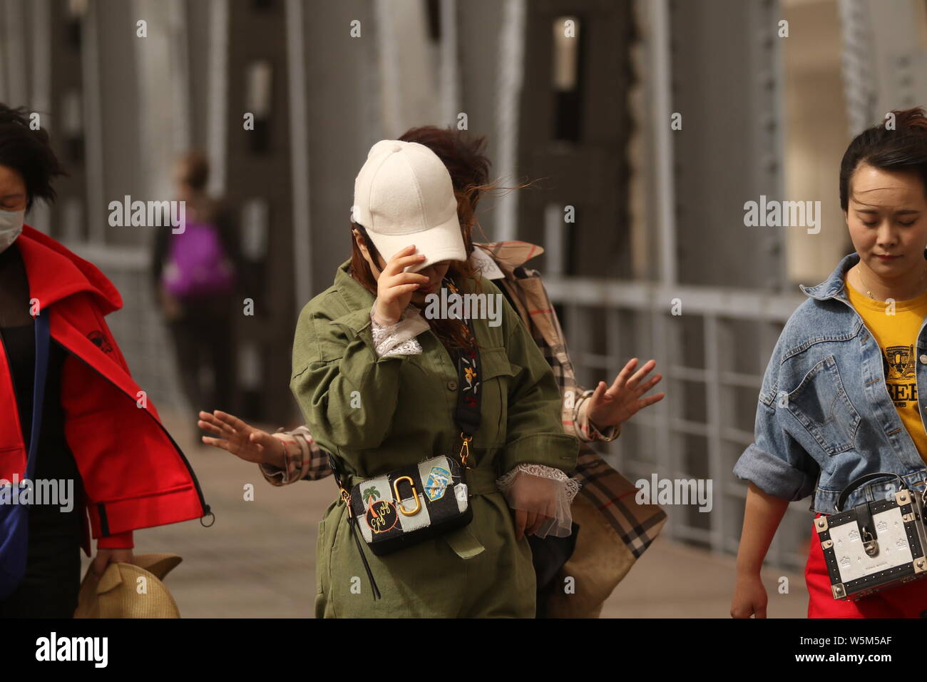 A pedestrian covers her head with hat against air pollution and strong ...