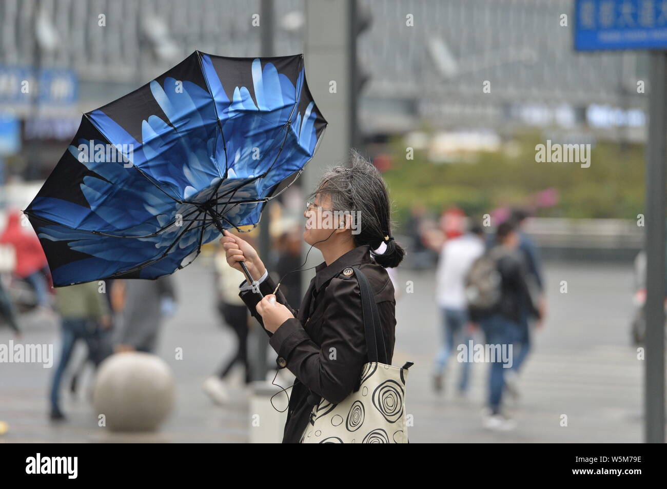 High wind breaks an umbrella and tumbles a woman's hair as wind and ...