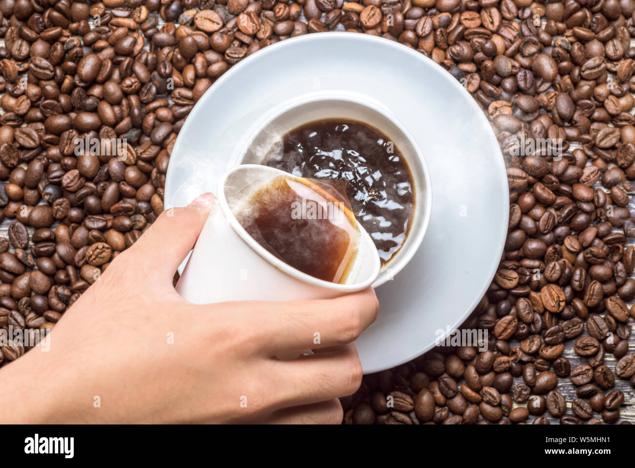 Hand pouring the coffee from styrofoam cup to the mug cup with coffee ...